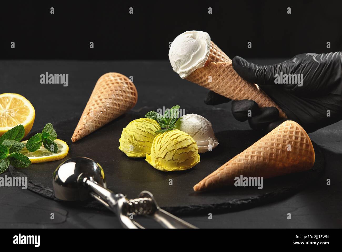 Hand in a dark glove is holding a waffle cone with a creamy ice cream ...