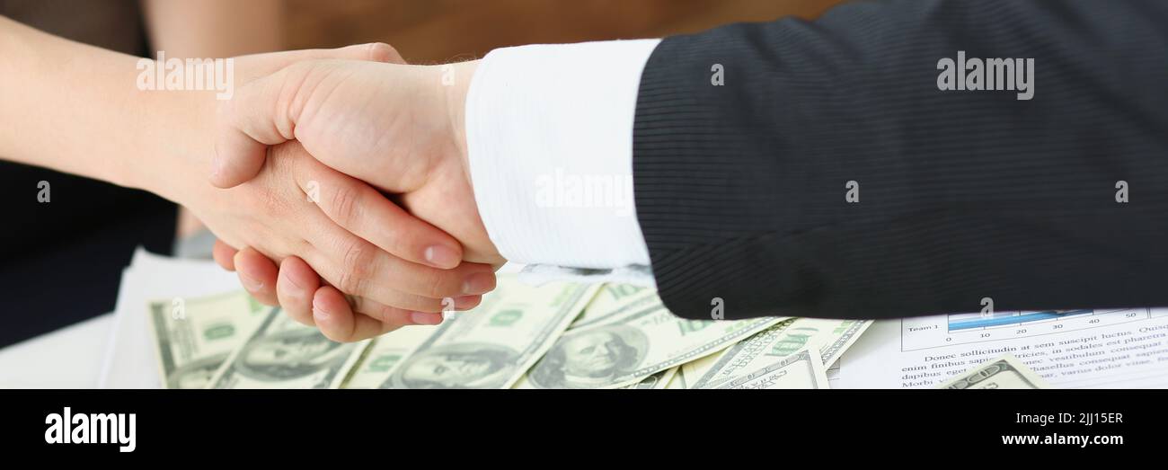 Businesspeople shake hands over bunch of dollar banknotes, transaction ...