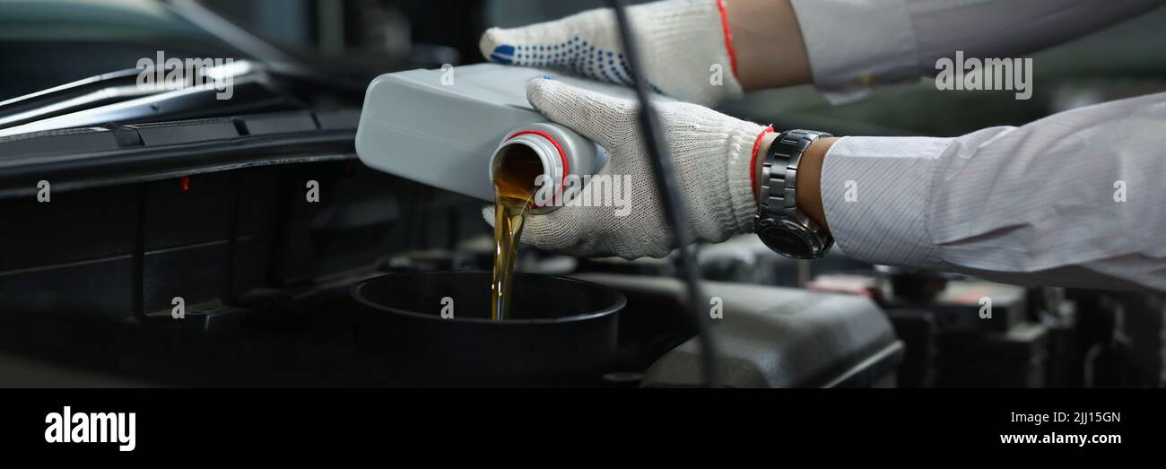 Worker refueling and pouring new oil into engine motor of automobile ...