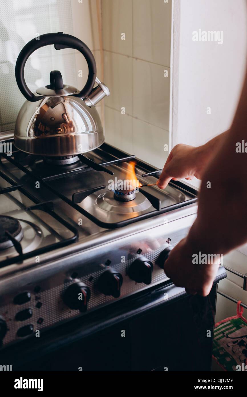 A man's hand with a match lights a gas burner or a gas stove in the ...