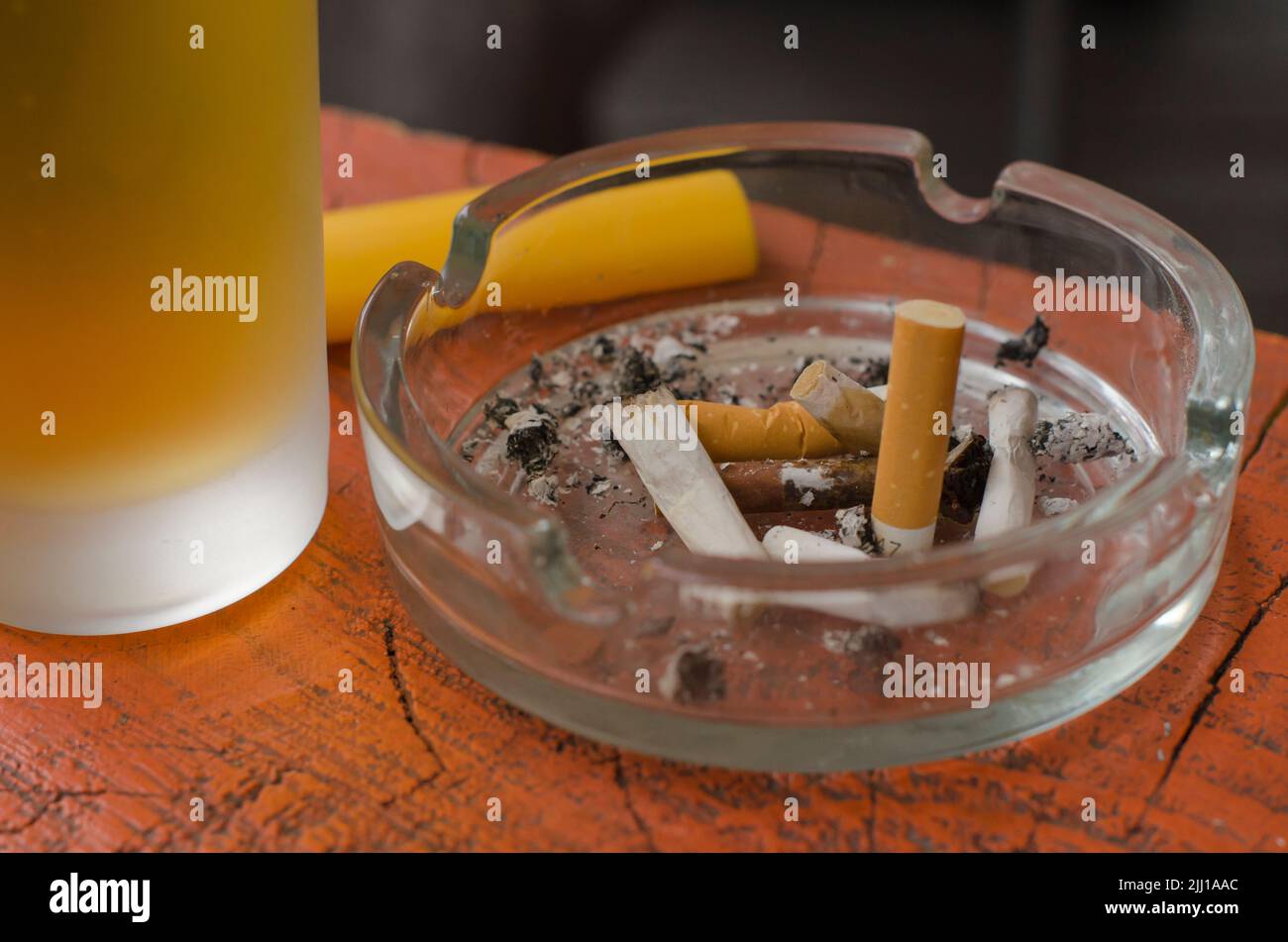 Frosty beer cigarettes in ashtray and a lighter on a timber table ...