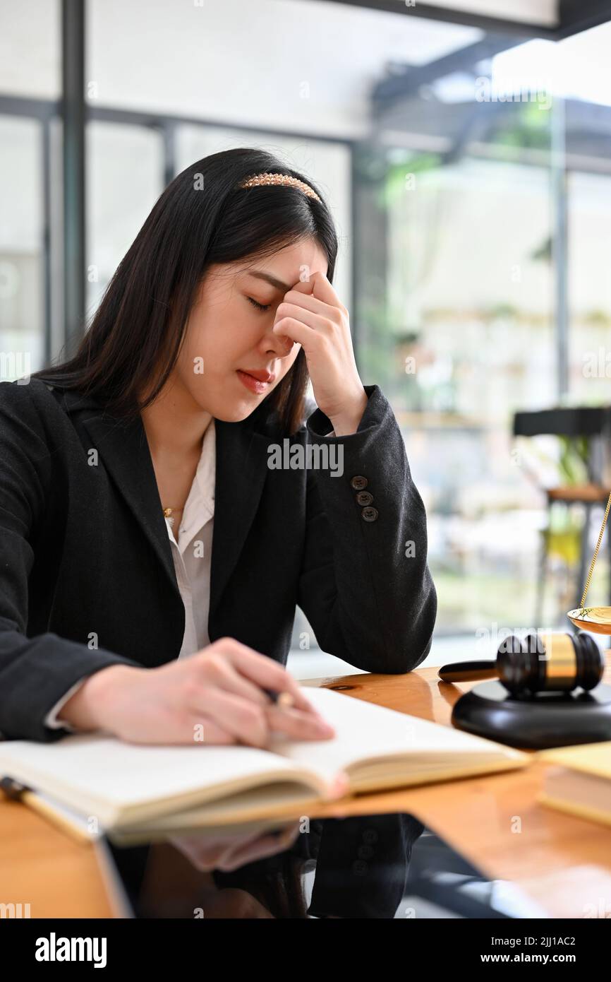 Stressed young Asian female lawyer sits at her desk in the office ... Stressed young Asian female lawyer sits at her desk in the office ...
