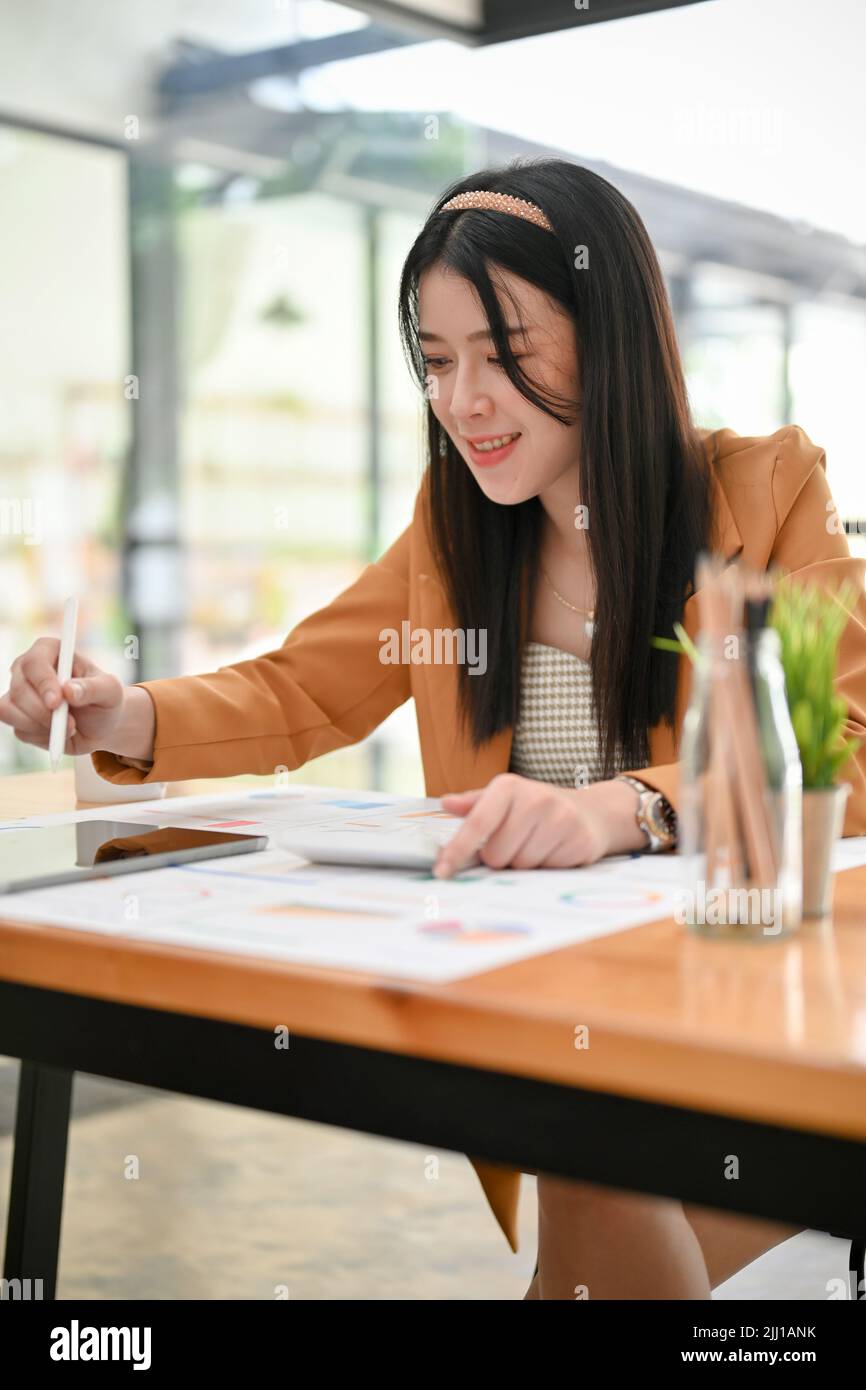 Charming young Asian female finical employee working on her financial ... Charming young Asian female finical employee working on her financial ...