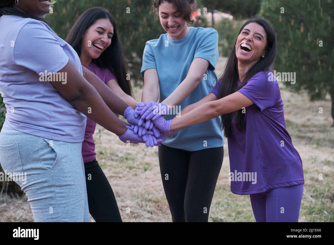 Group of multiracial active women laugh and put hands together after ...