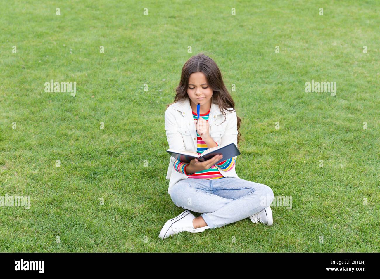 pondering teen girl making notes in notebook sitting on grass. taking ...