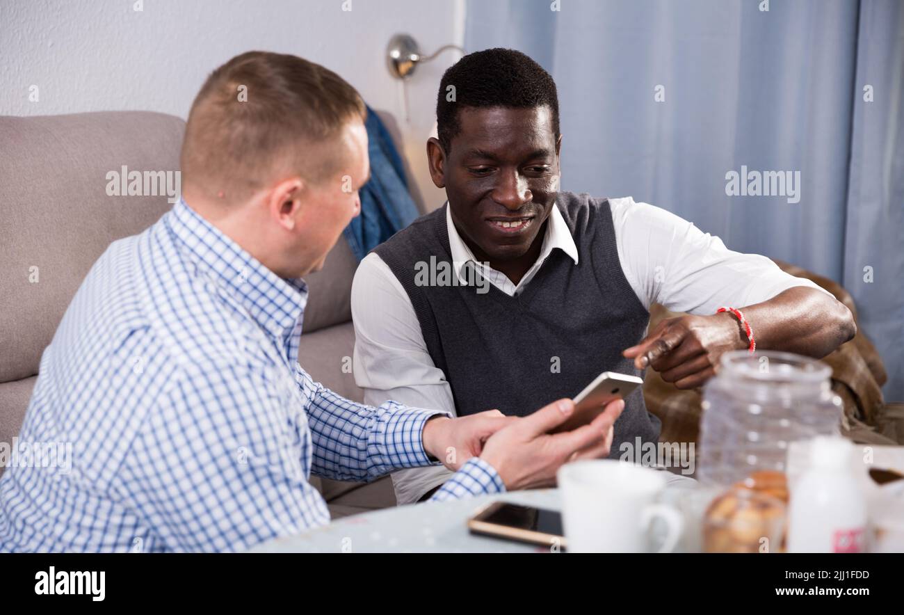 Two smiling male friends with smartphones and talking Stock Photo - Alamy