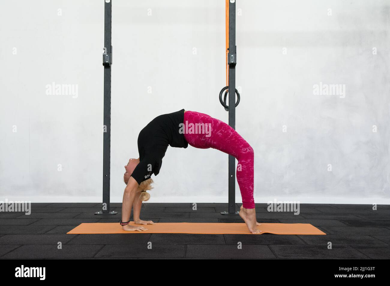 Youth blonde woman performing chakrasana, advanced back bending with ...
