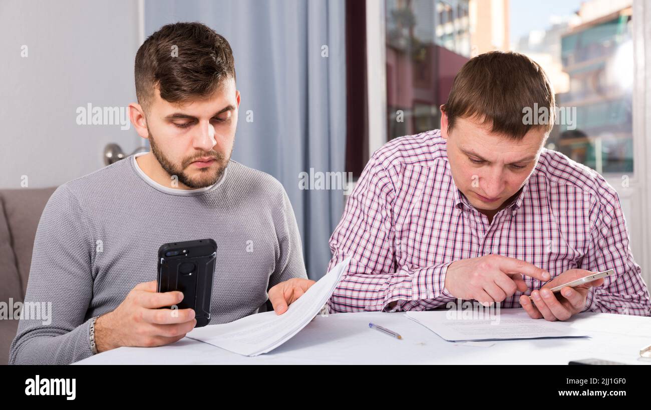 Serious males with documents and phone at home table Stock Photo - Alamy