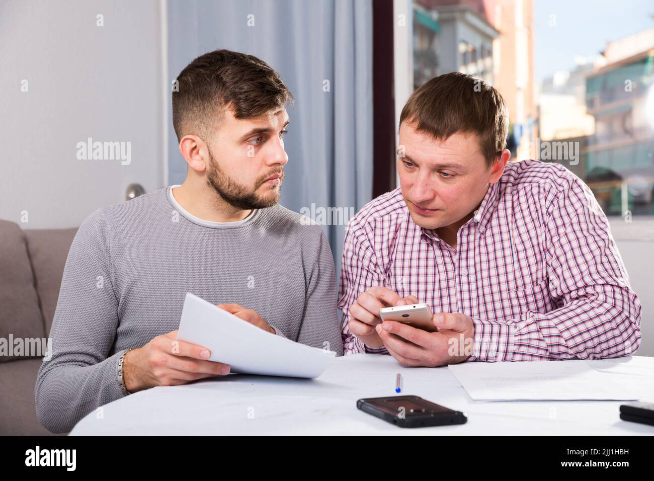 Serious men with documents and phone at home table Stock Photo - Alamy