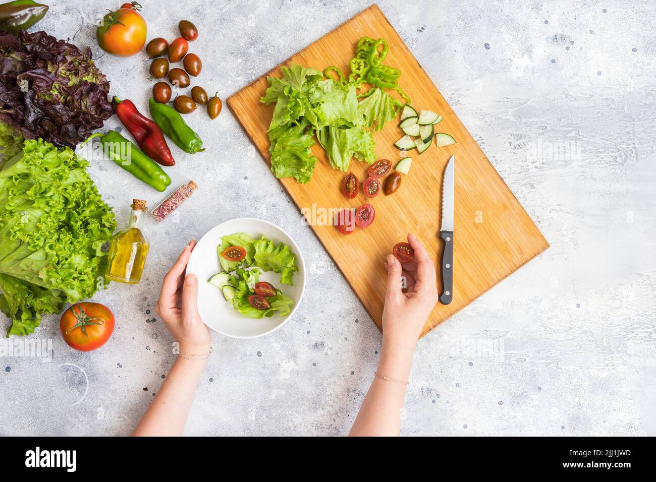 Woman hands are putting cut vegetables in a salad bowl on wooden desk ...