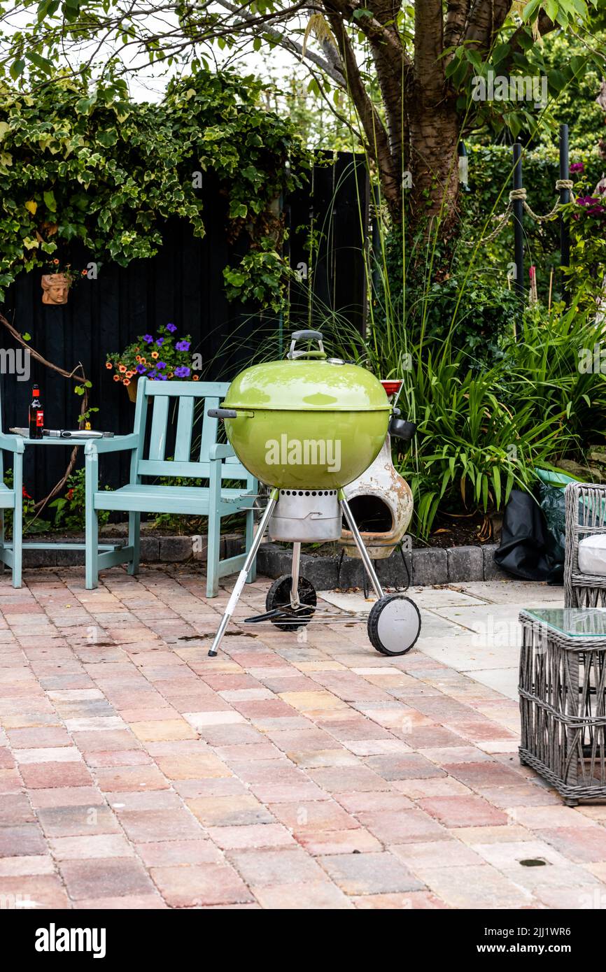 Green kettle barbeque on a stone / tiled patio, with chair and table ...