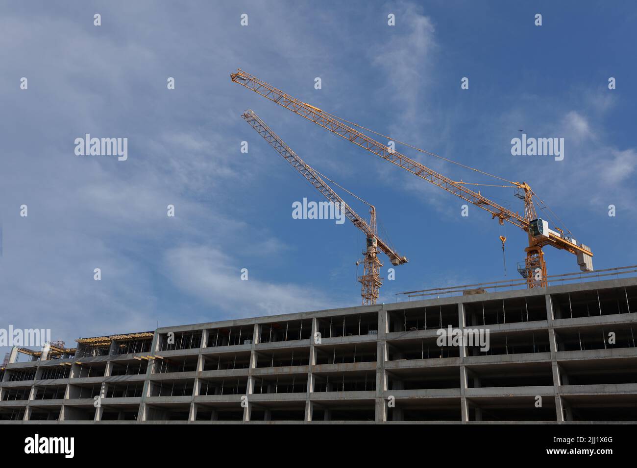 Construction site with incomplete building and two cranes high up in ...