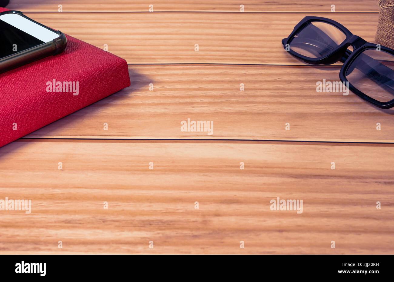 Cellphone, red note book, potted plant and reading glasses on wooden ...