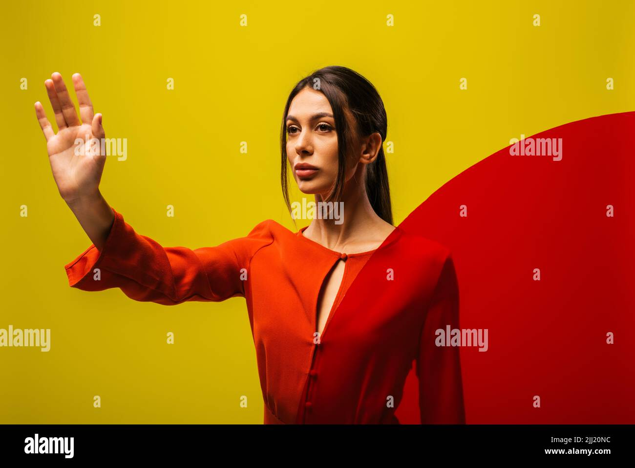 stylish young woman in red dress showing stop sign near round shape ...