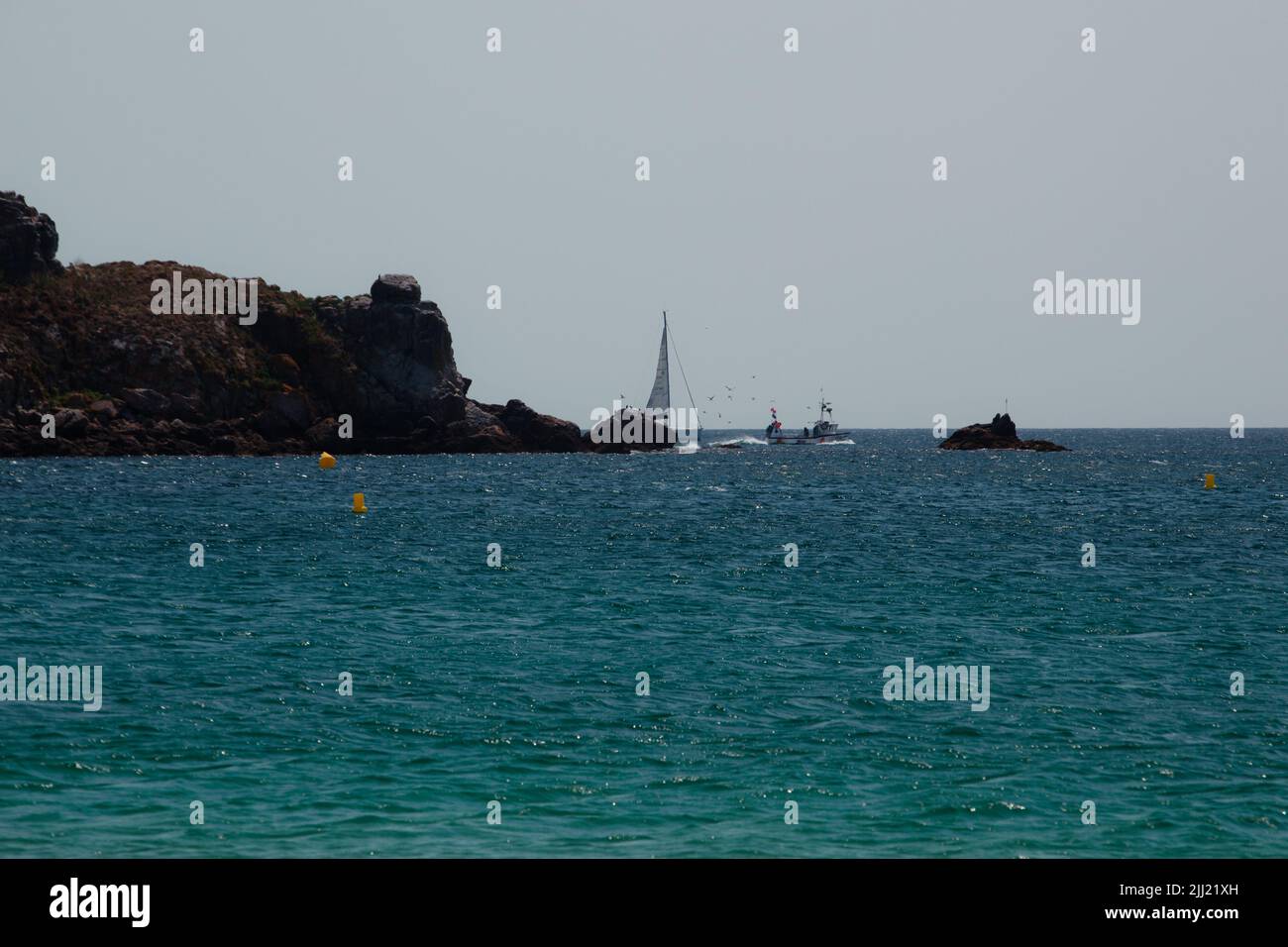 a sailboat and a fishing boat in the distance are passing between a ...