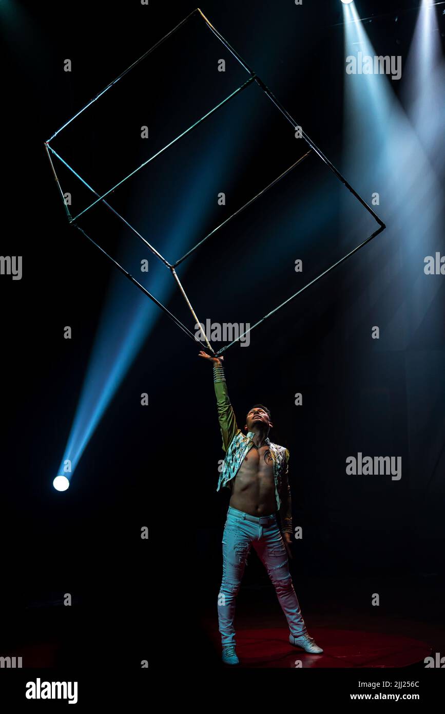 A vertical shot of a circus performer balancing a cube on his hand at ...