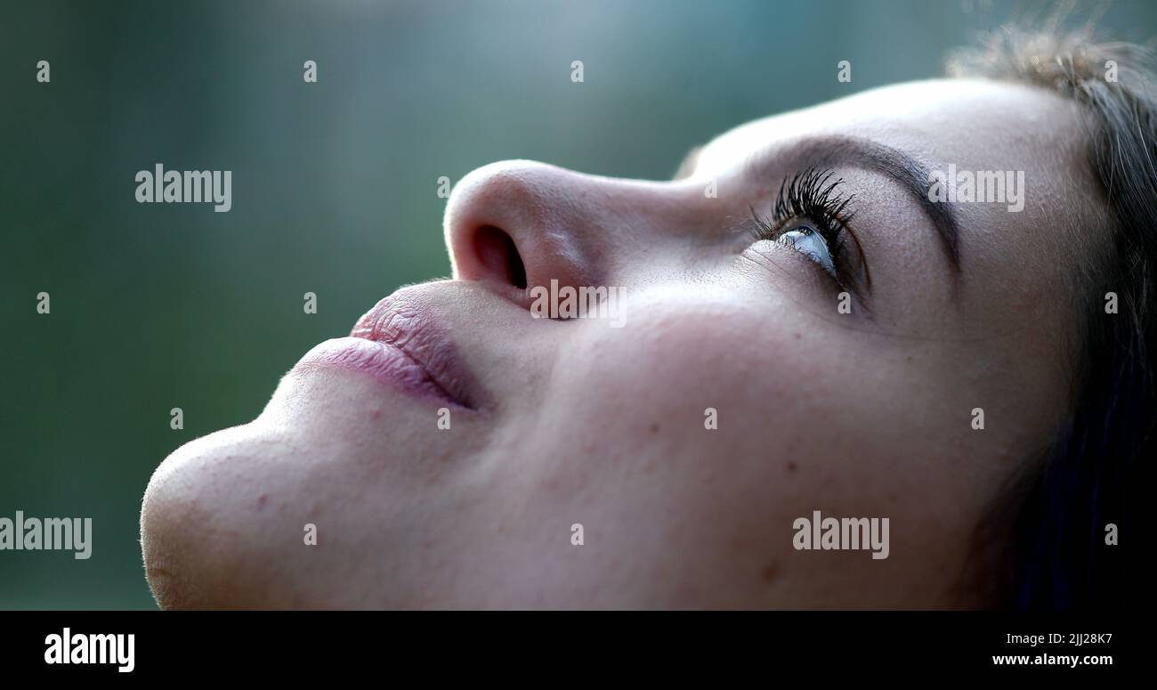 Young woman closing eyes and taking a deep breath, looking up to sky ...