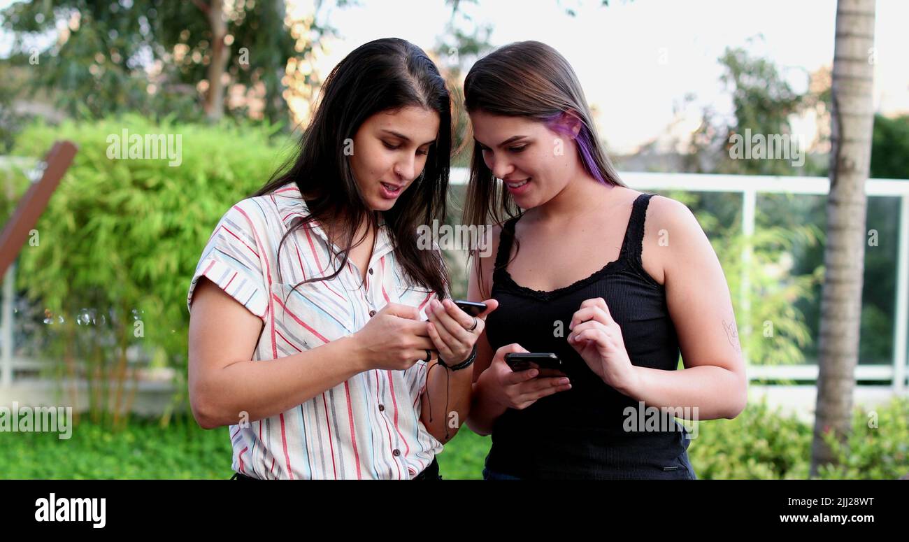 Young women standing outside using cellphone device smiling and ...