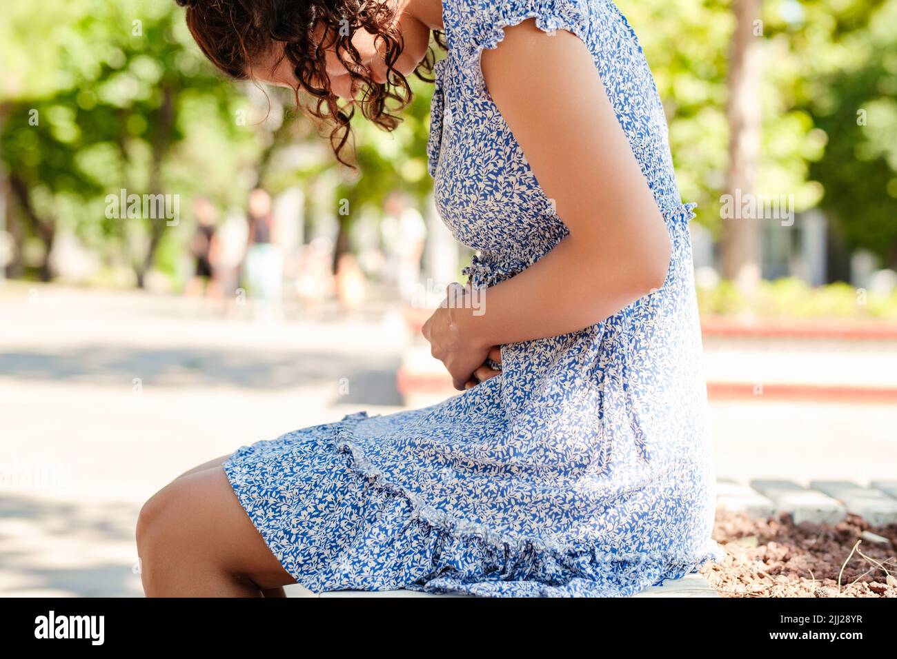 Side view of brunette woman wearing summer dress standing on city park ...