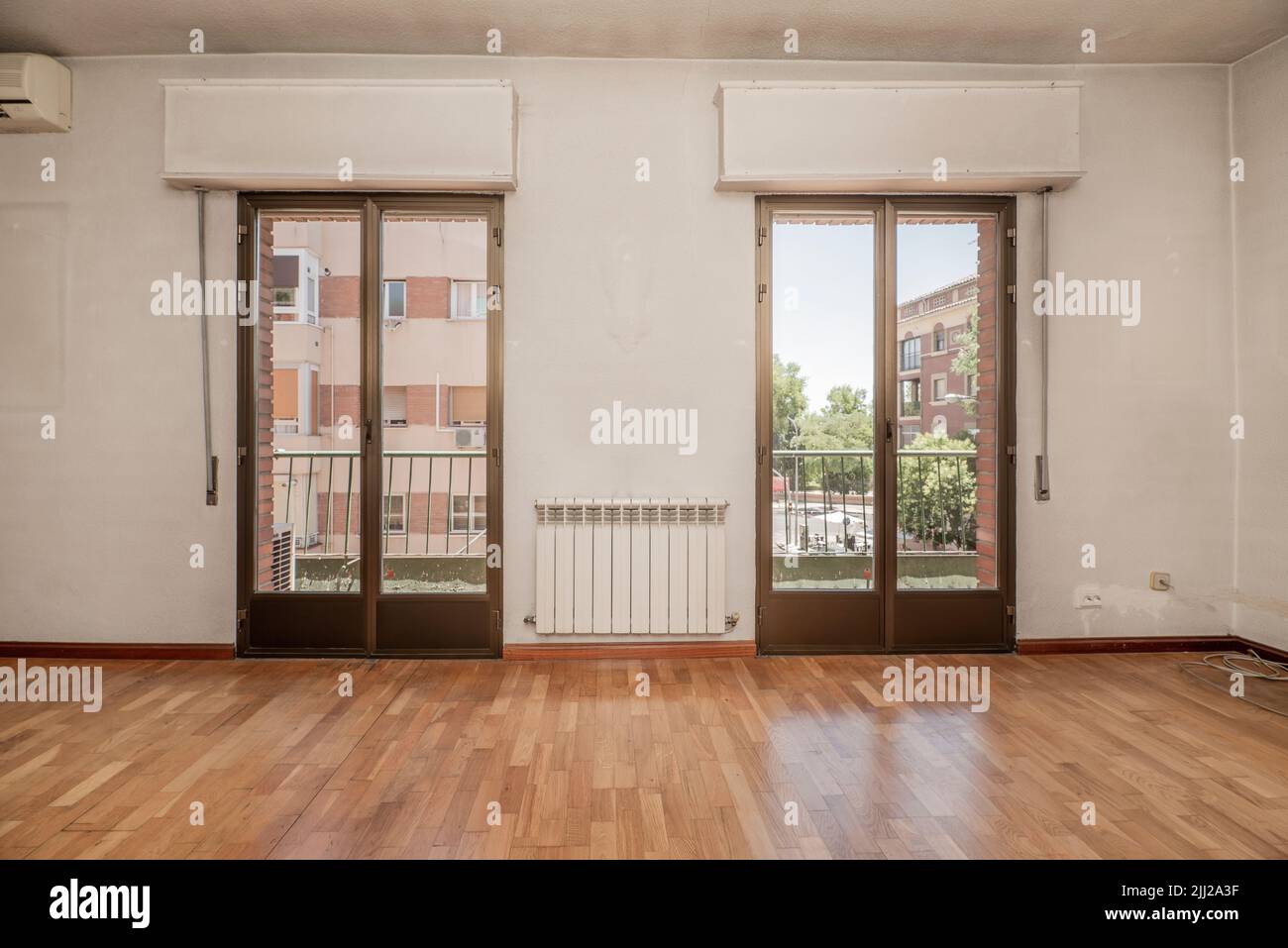 Empty living room with oak wood floor, white painted walls, and two ...
