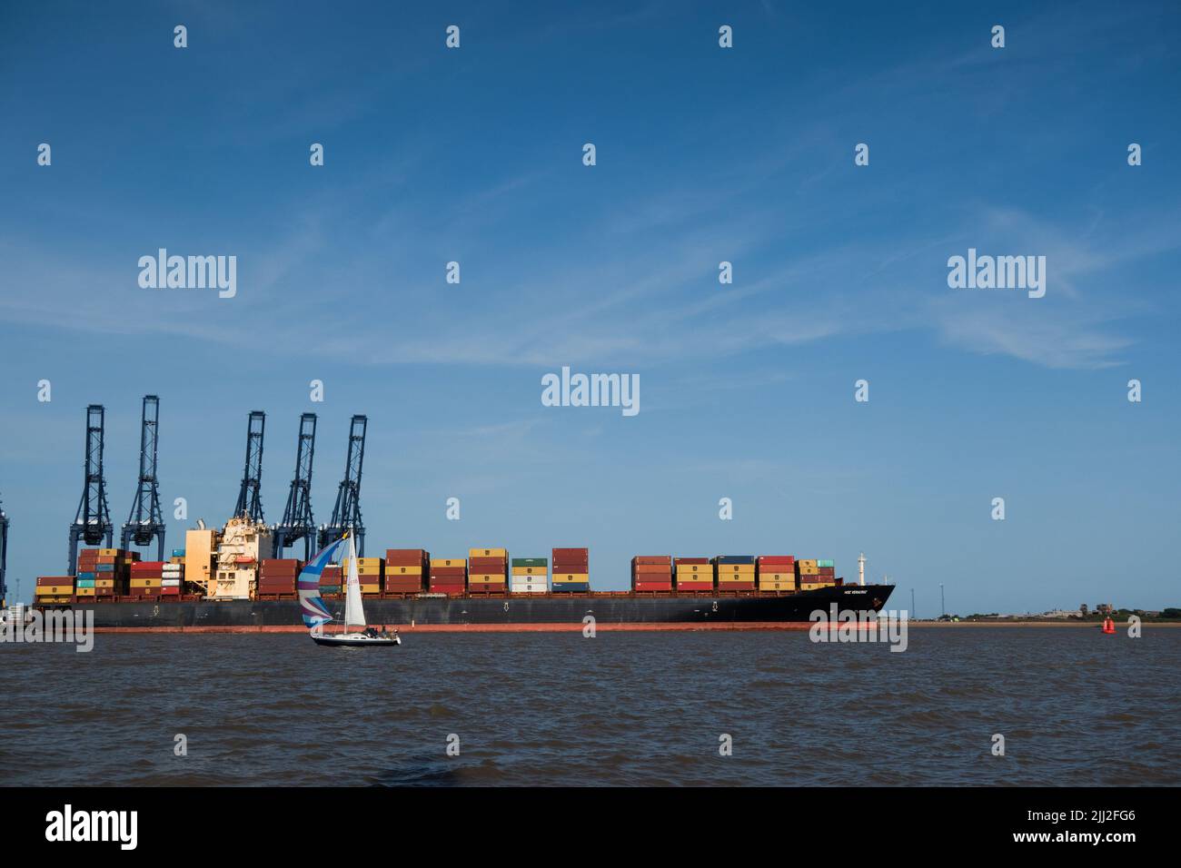 Small yacht flying spinnaker alongside a massive container ship leaving ...