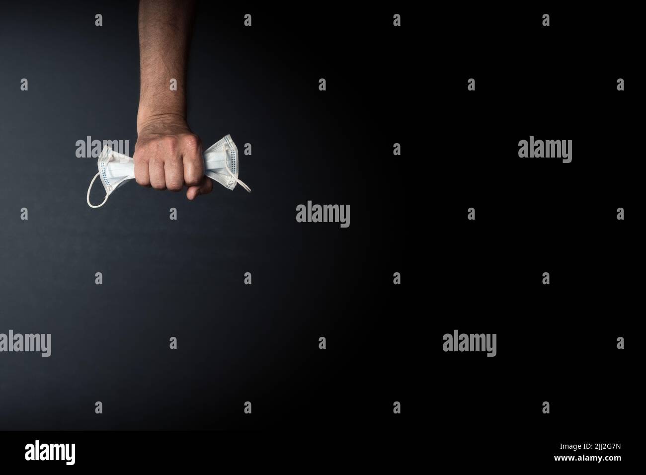 clenched male fist holding crumpled covid medical mask against dark ...