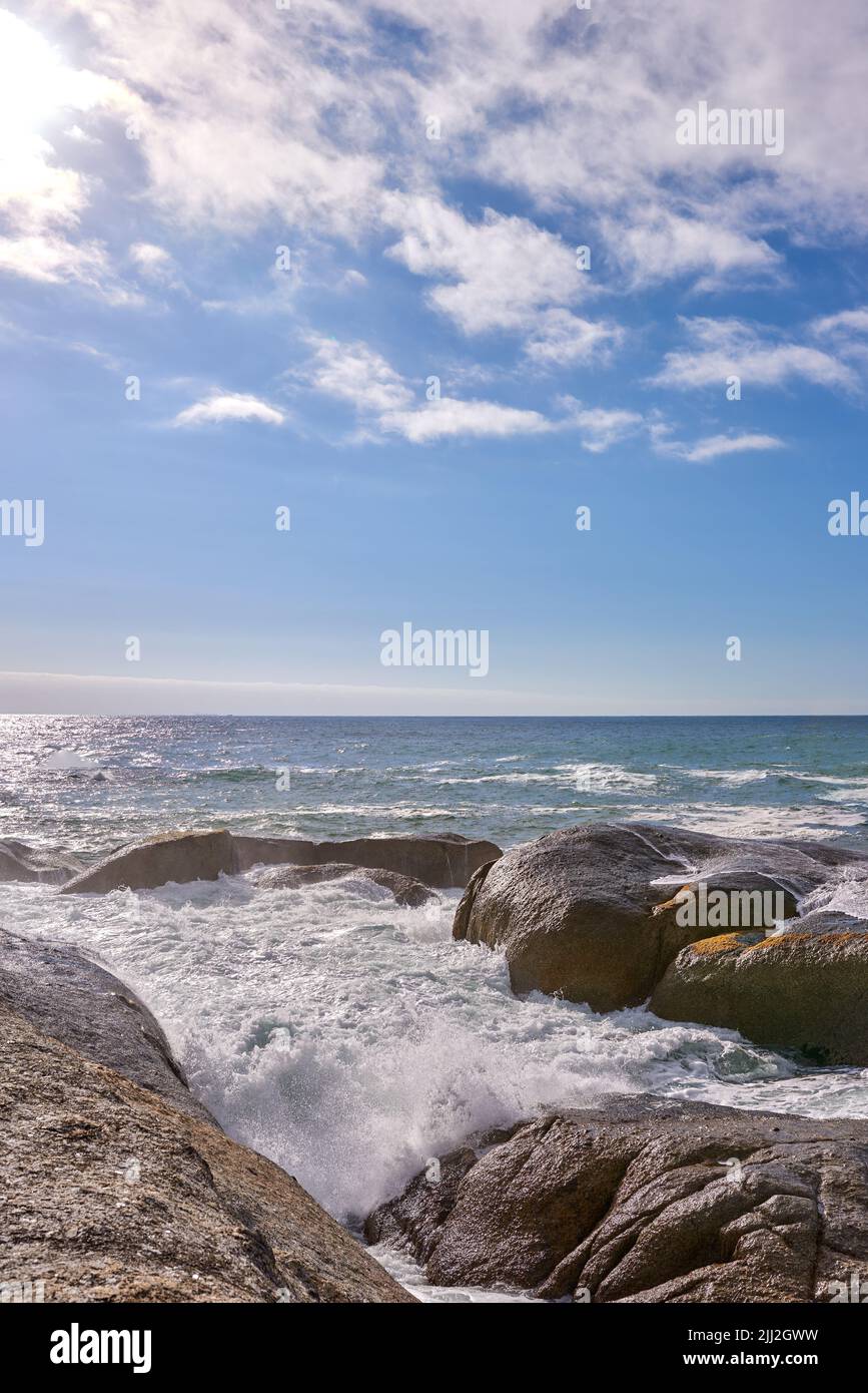 Waves crashing against rocks in the ocean under a blue cloudy sky with ...