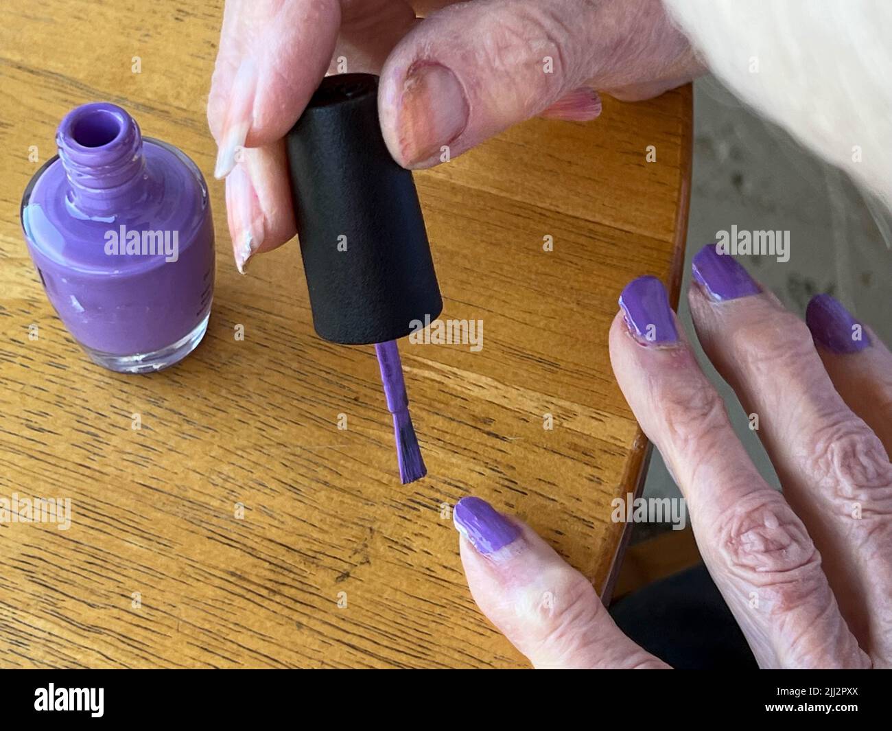 Elderly senior grandmother polishing her fingernails with purple polish ...