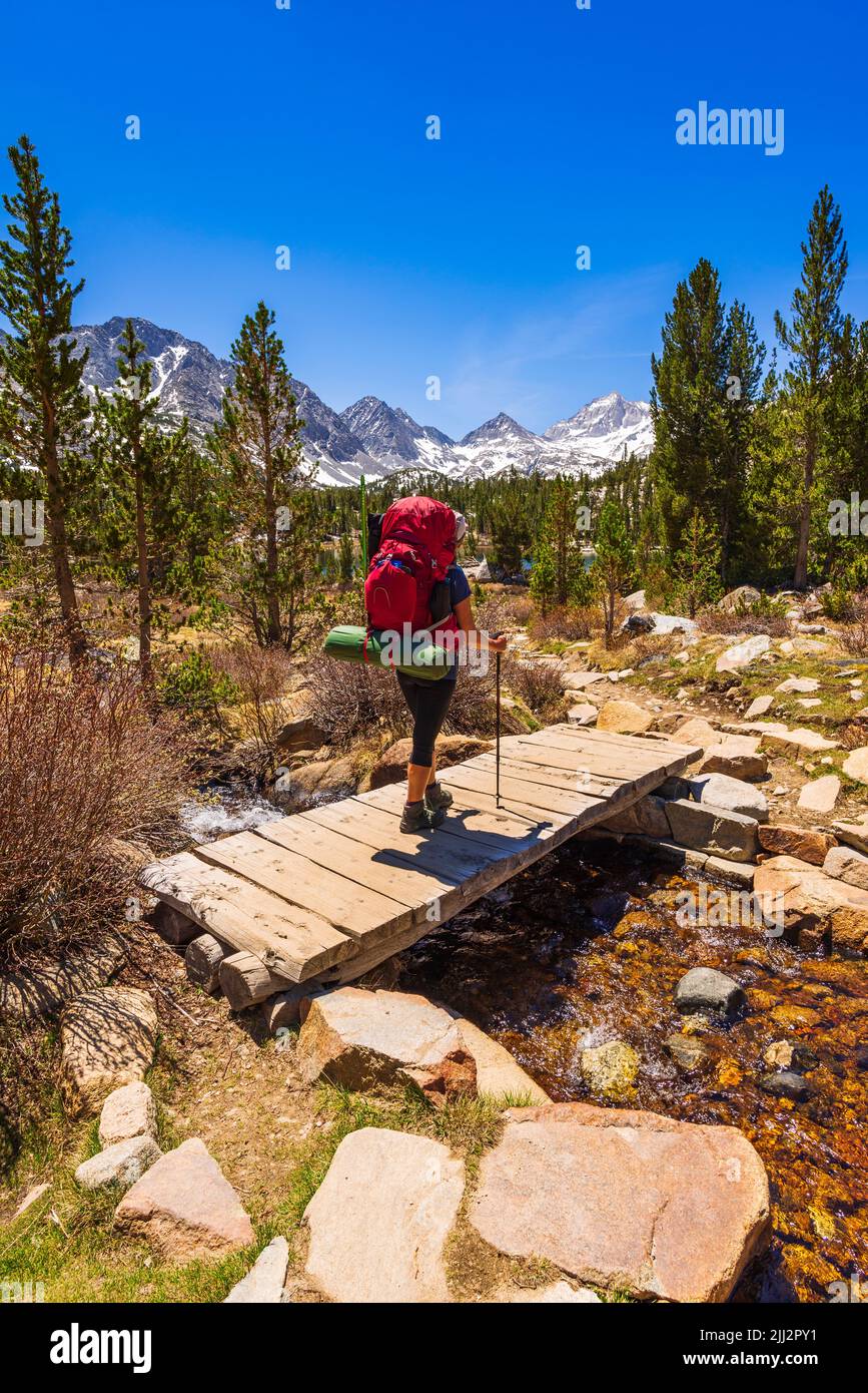 Woman crossing footbridge over mountain stream in Little Lakes Valley ...