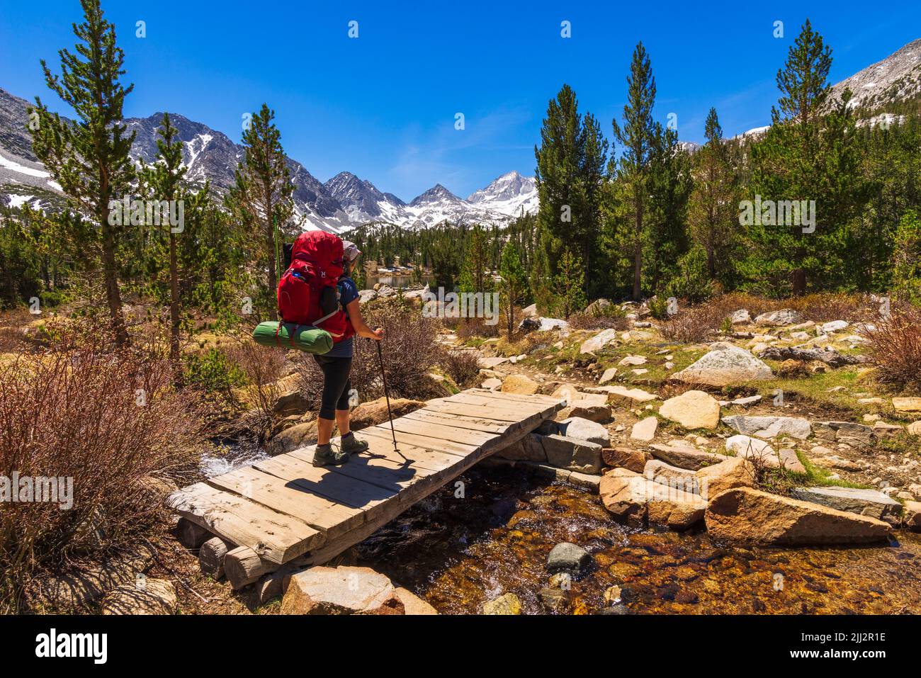 Woman crossing footbridge over mountain stream in Little Lakes Valley ...