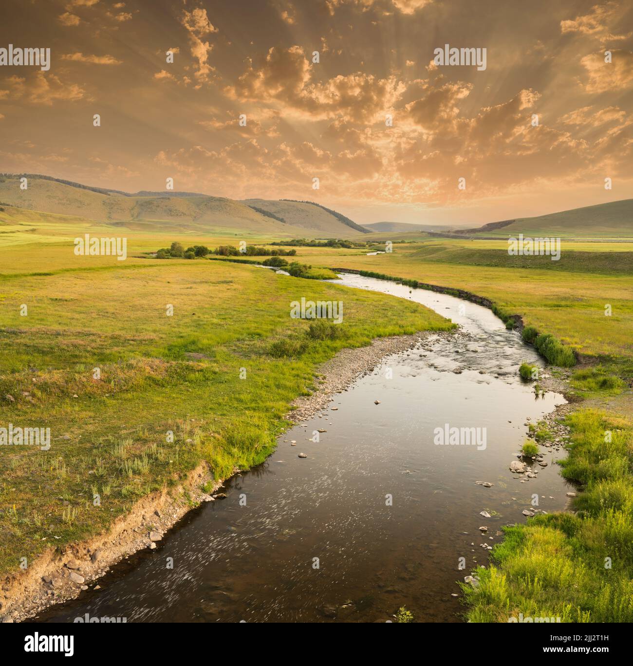 The small river flows towards the hills at sunset. Stream flowing ...