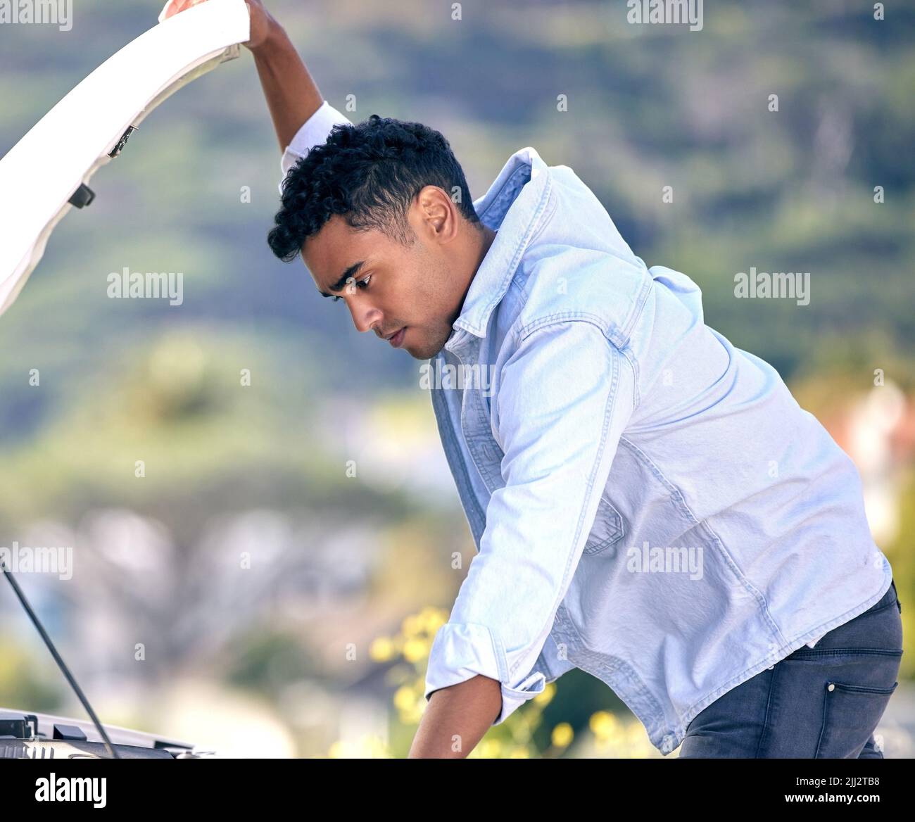 I wonder what the problem is... a handsome young man checking under the hood of his car after ...