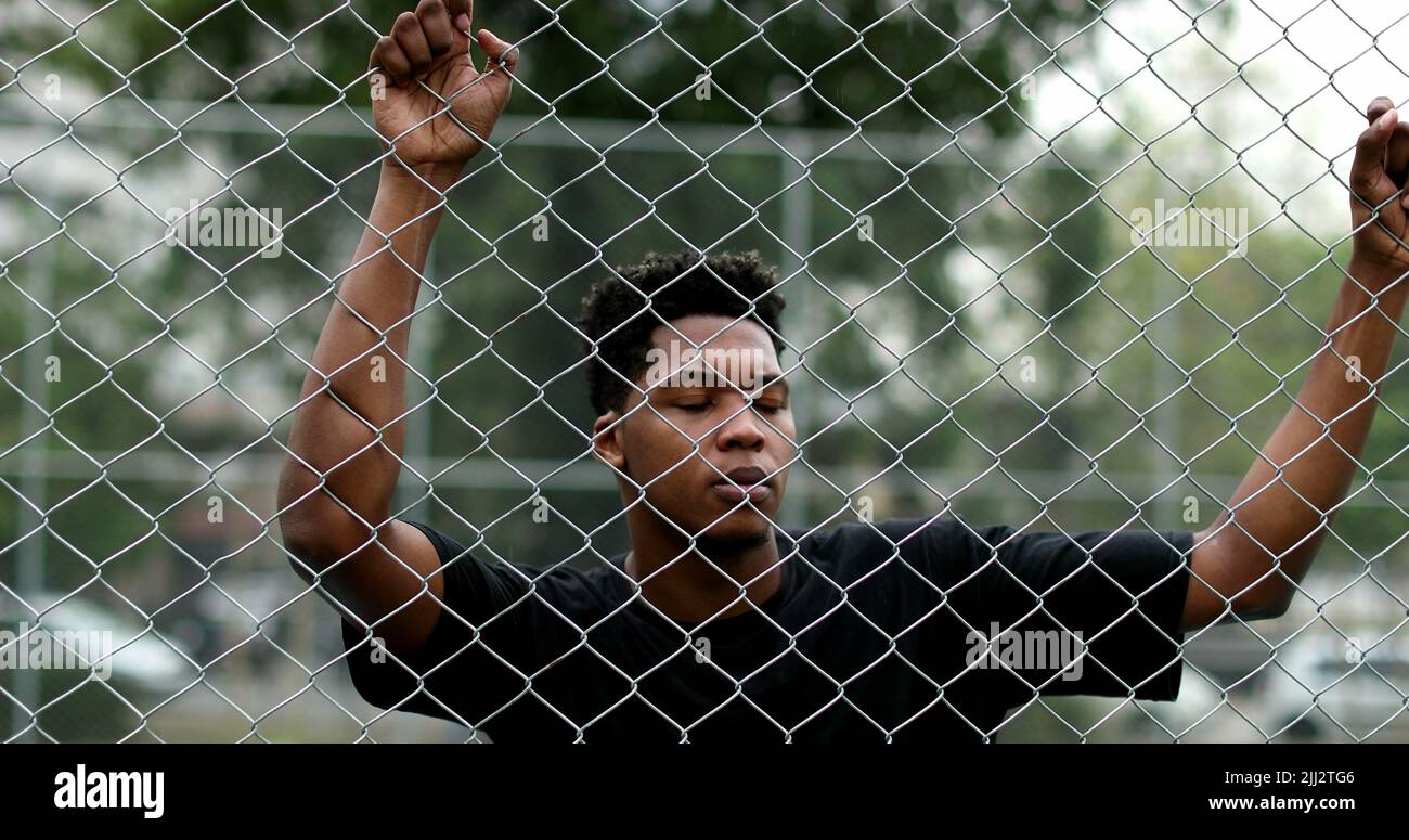 Pensive young black man leaning on metal fence. Contemplative mixed ... Pensive young black man leaning on metal fence. Contemplative mixed ...