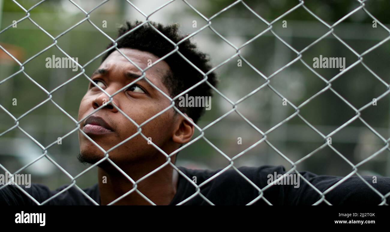 Pensive young black man leaning on metal fence. Contemplative mixed ... Pensive young black man leaning on metal fence. Contemplative mixed ...