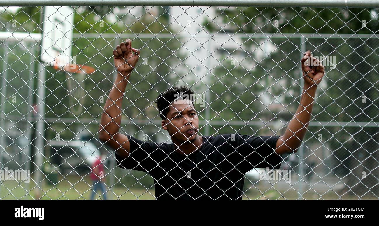 Pensive young black man leaning on metal fence. Contemplative mixed ... Pensive young black man leaning on metal fence. Contemplative mixed ...