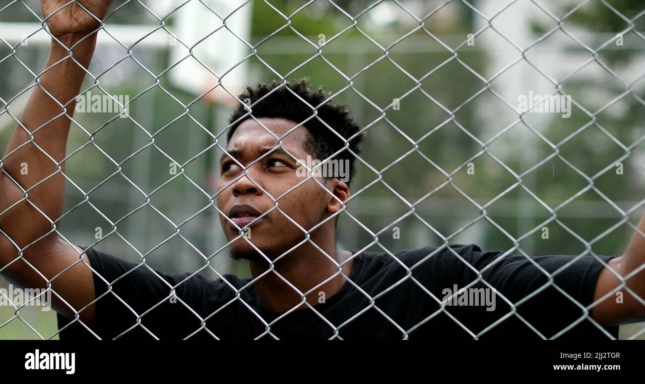 Pensive young black man leaning on metal fence. Contemplative mixed ... Pensive young black man leaning on metal fence. Contemplative mixed ...