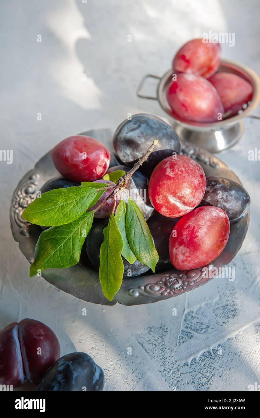 antique silver bowl filled with red plums on a rustic table ...