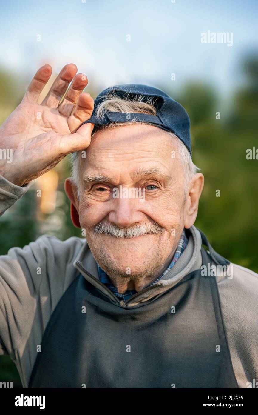 Portrait of an 88-year-old man in a baseball cap with his hand raised ...