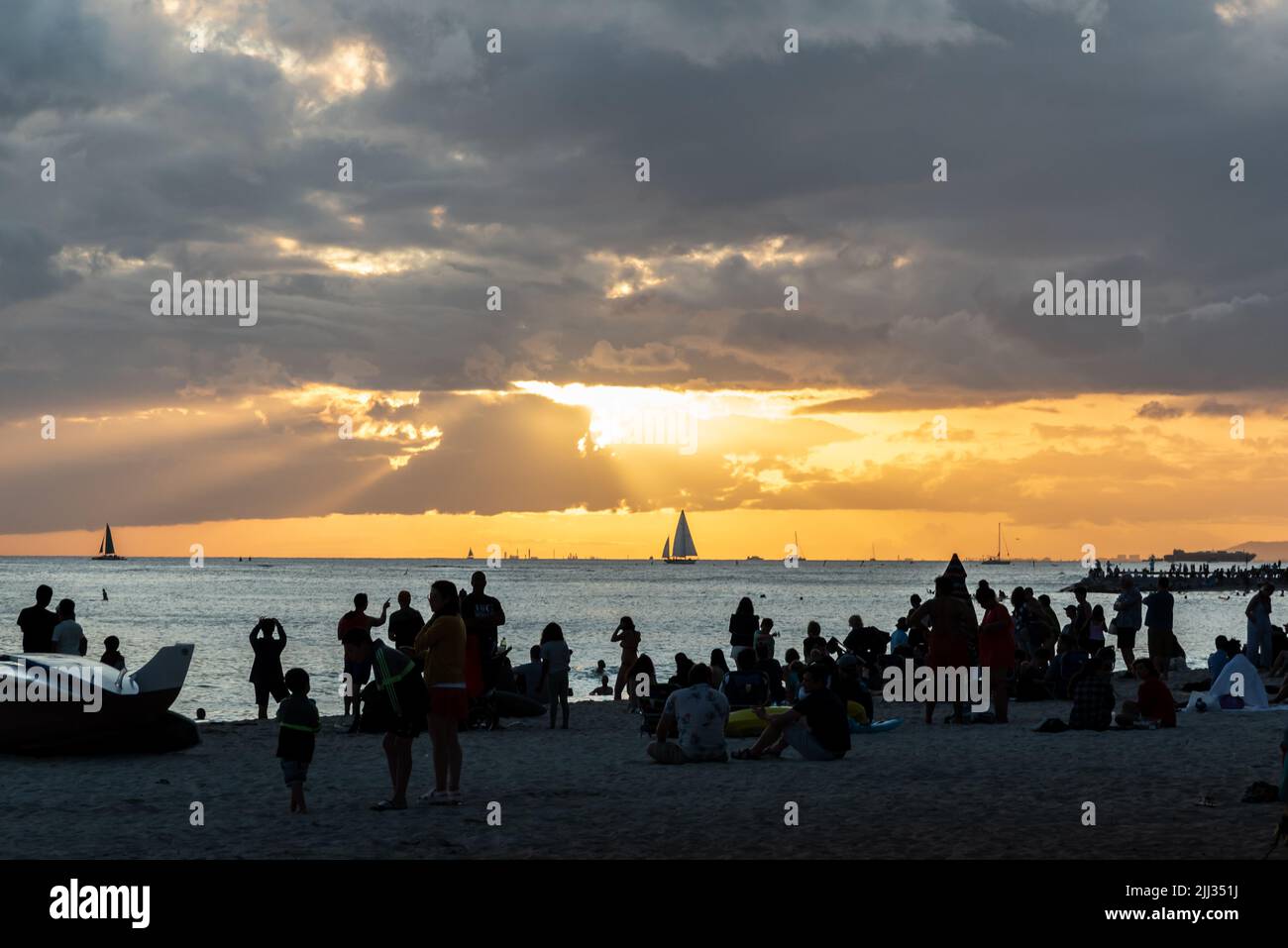 Sunset on Waikiki Beach with tourist watching the sun dip below the ...