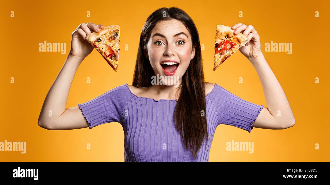 Excited girl invites you for pizza, holds two slices in hands and looks ...