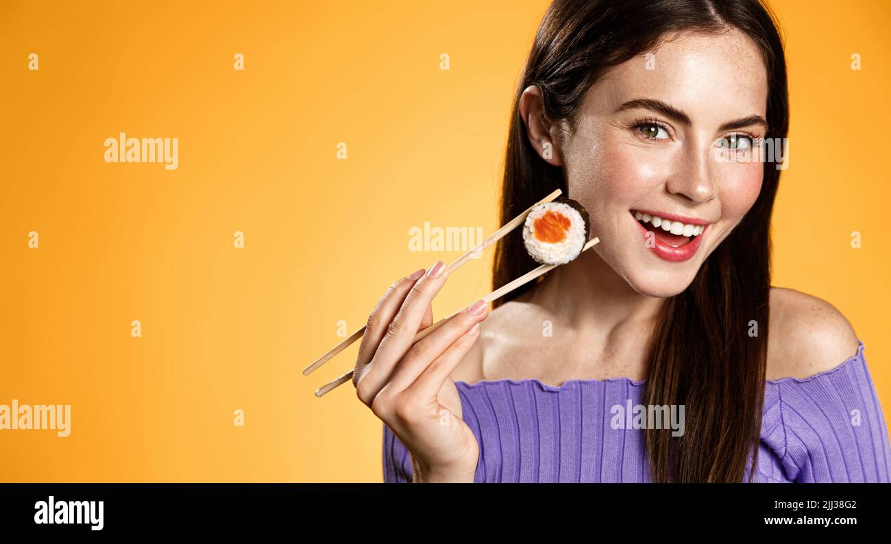 Happy woman poses with salmon sushi roll and chopsticks, eating asian ...