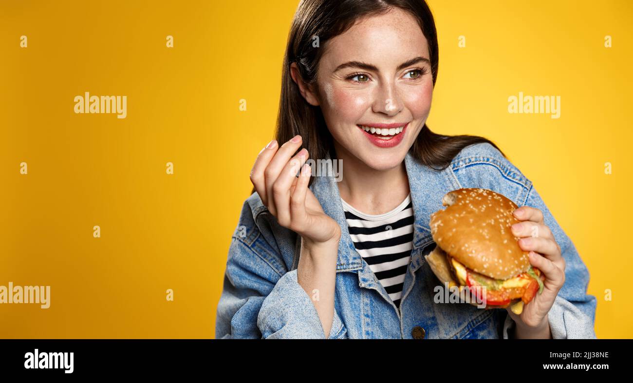 Young woman smiling, casually eating delicious burger. Girl bites ...