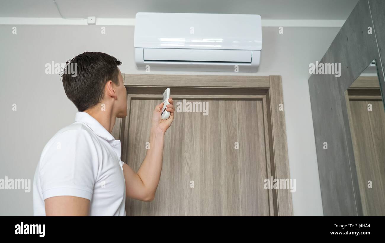 Man turns on air conditioner with remote control in hot room Stock ...