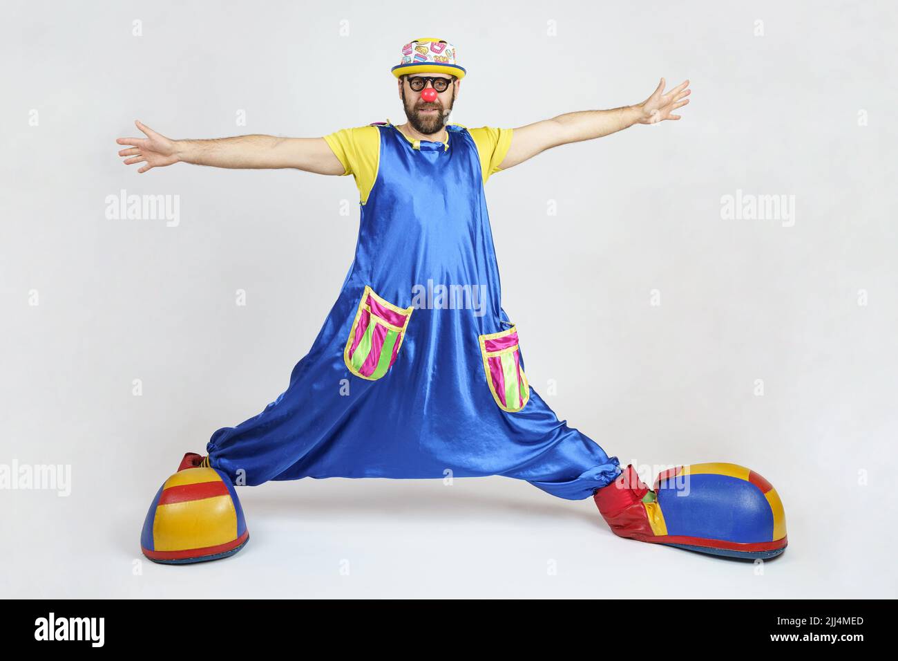 Humor and fun concept. A clown in a bright costume stands with his arms ...