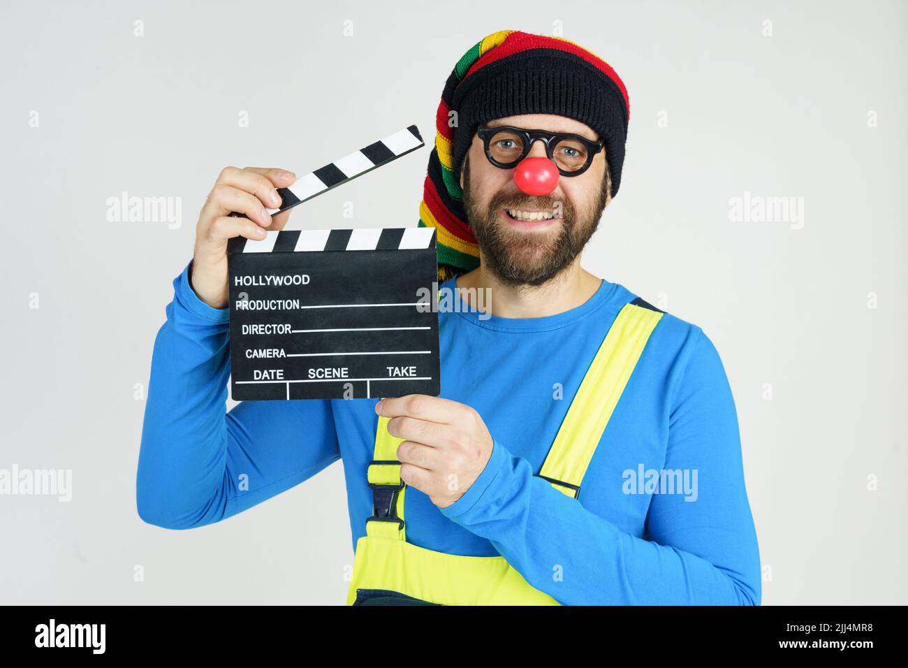 Humor and fun concept. A clown in a bright suit holds a movie ...
