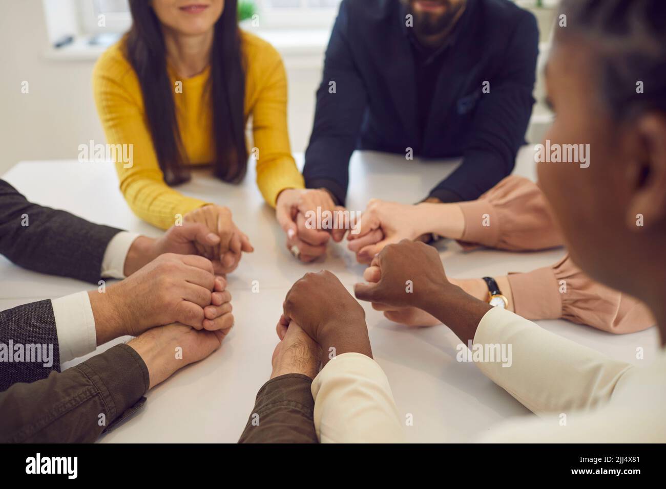 Diverse multiracial team of people sitting together around a table and holding hands Stock Photo ...