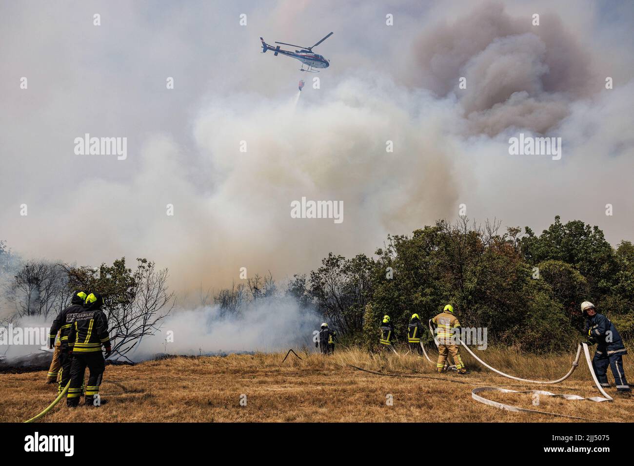 Firemen and a helicopter battle a large wildfire that burns near the ...