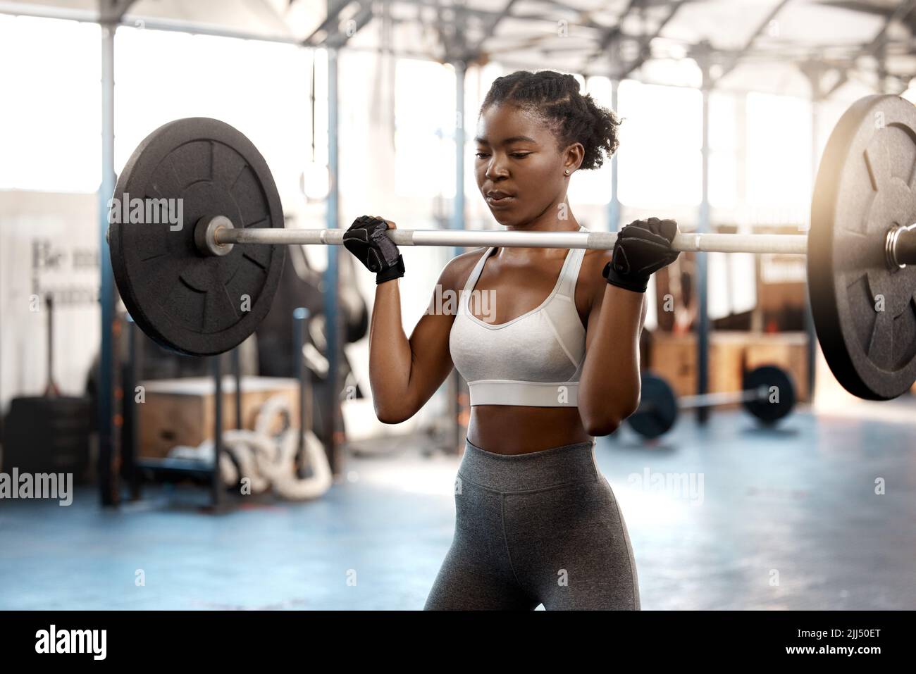 Strong women only intimidate weak men. a sporty young woman exercising with a barbell in a gym ...