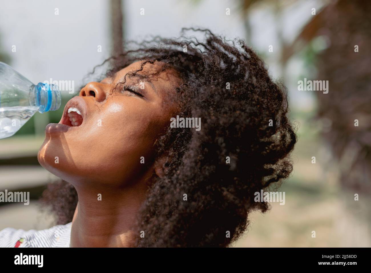 African woman hydrating and drinking water from a bottle on a hot day ...