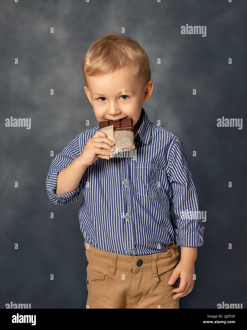 Portrait of small boy kid eating chocolate on grey background. Happy ...